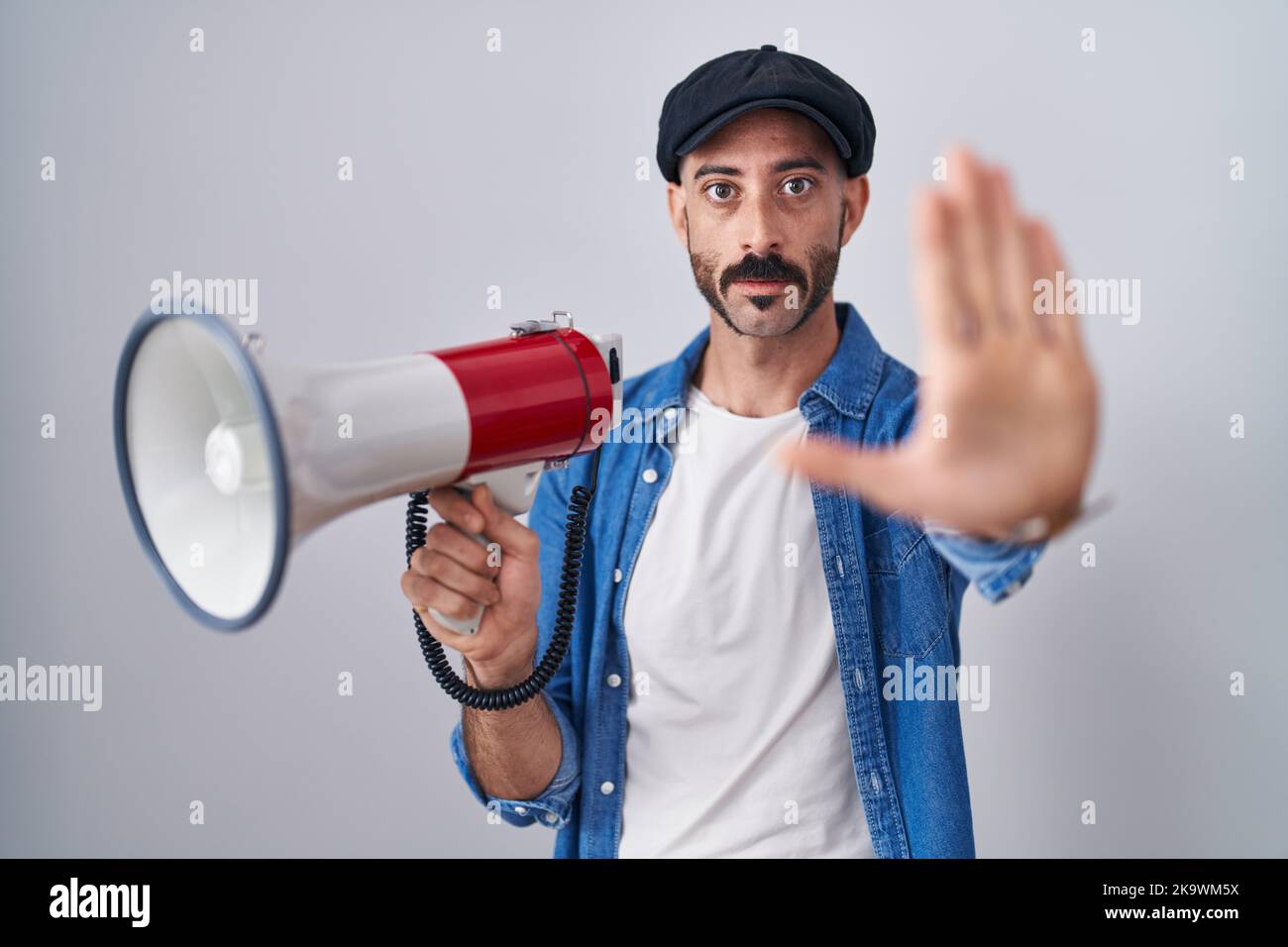 Hispanic man with beard shouting through megaphone with open hand doing ...