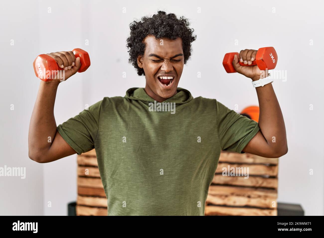 African man with curly hair wearing sportswear using dumbbells angry ...