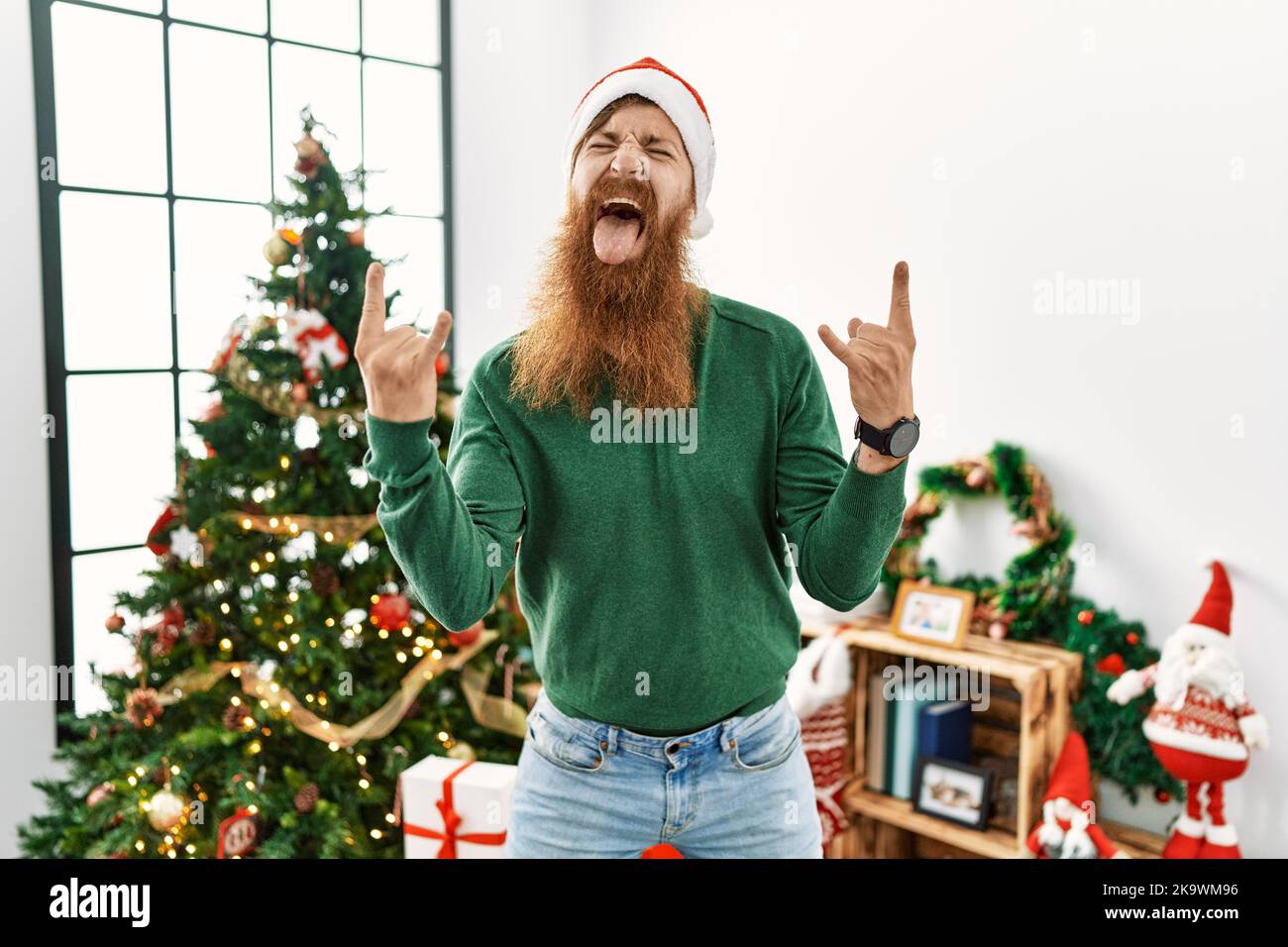Redhead man with long beard wearing christmas hat by christmas tree ...
