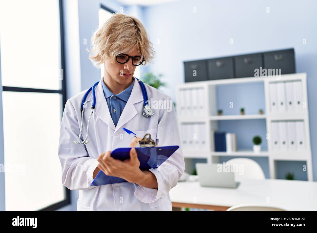 Young blond man doctor writing on document at clinic Stock Photo - Alamy