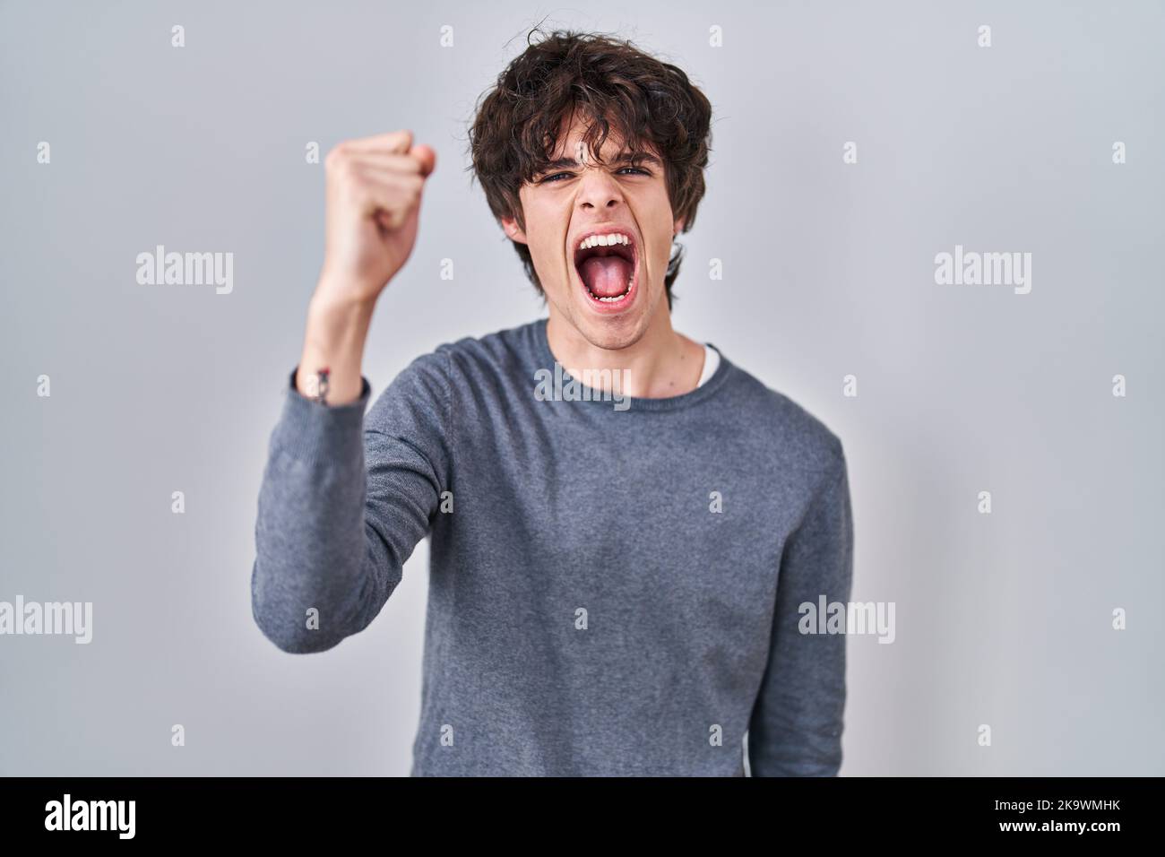 Young man standing over isolated background angry and mad raising fist ...