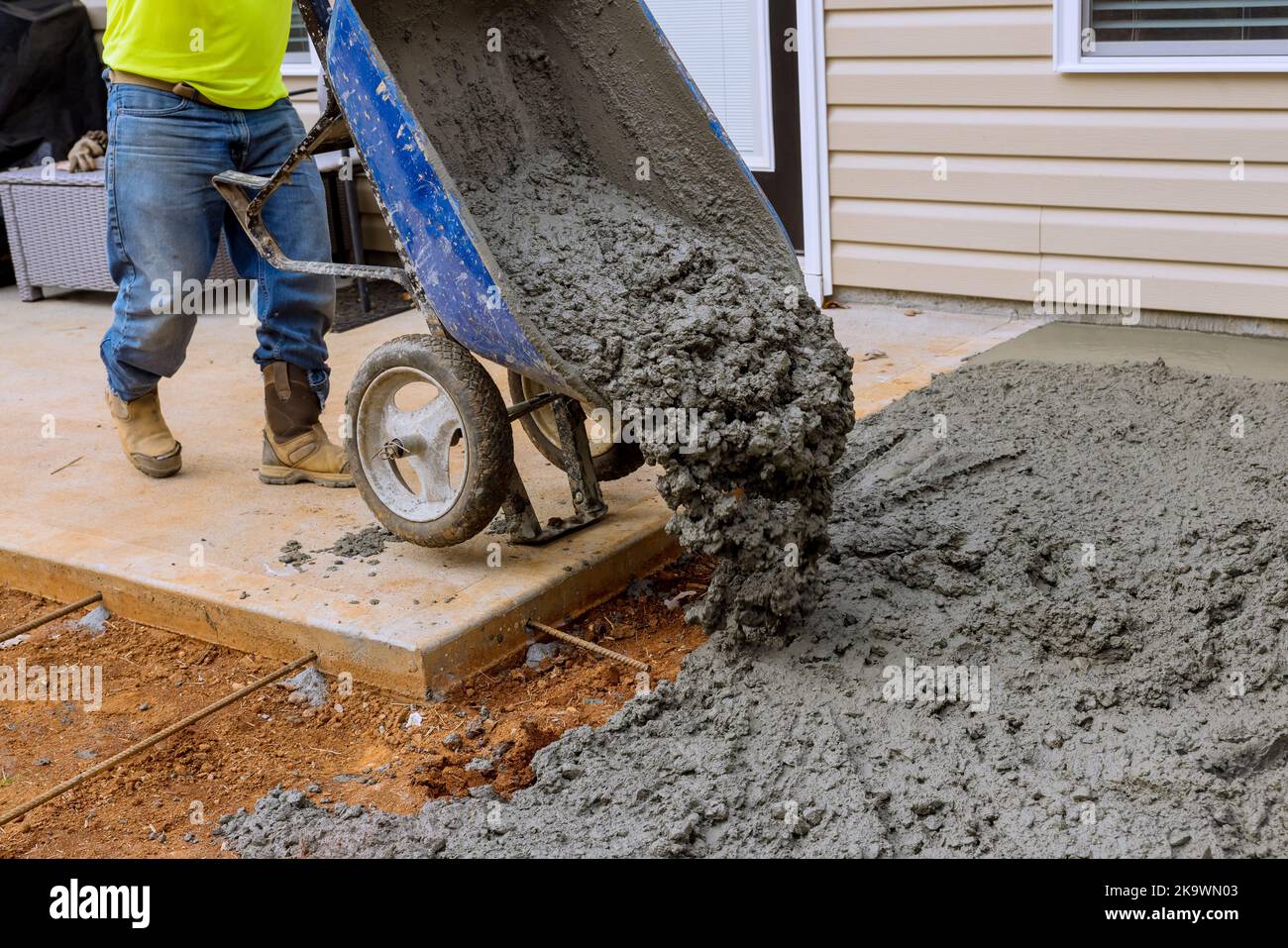 On side house construction worker pours cement from wheelbarrow to ...