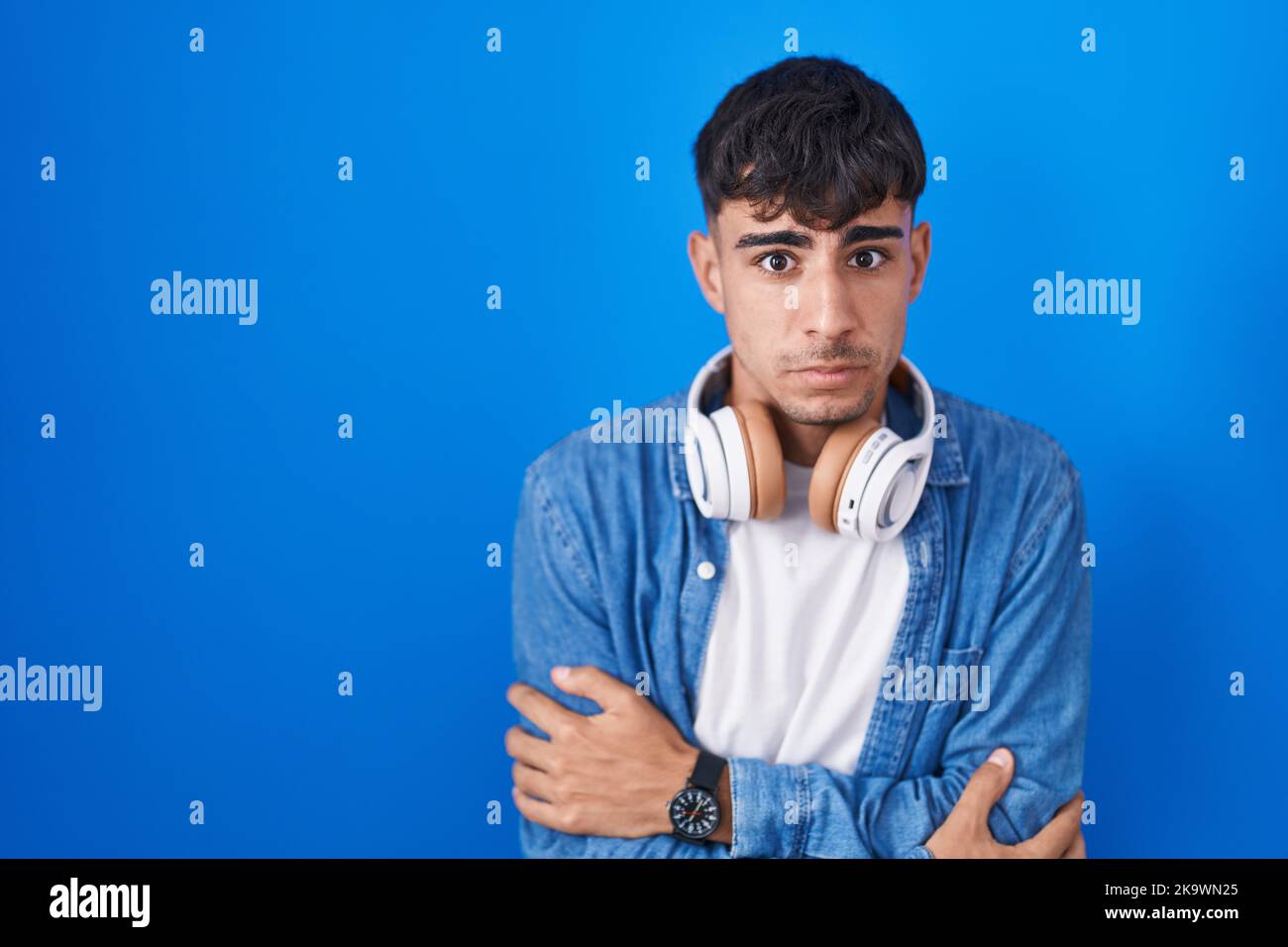 Young hispanic man standing over blue background shaking and freezing ...
