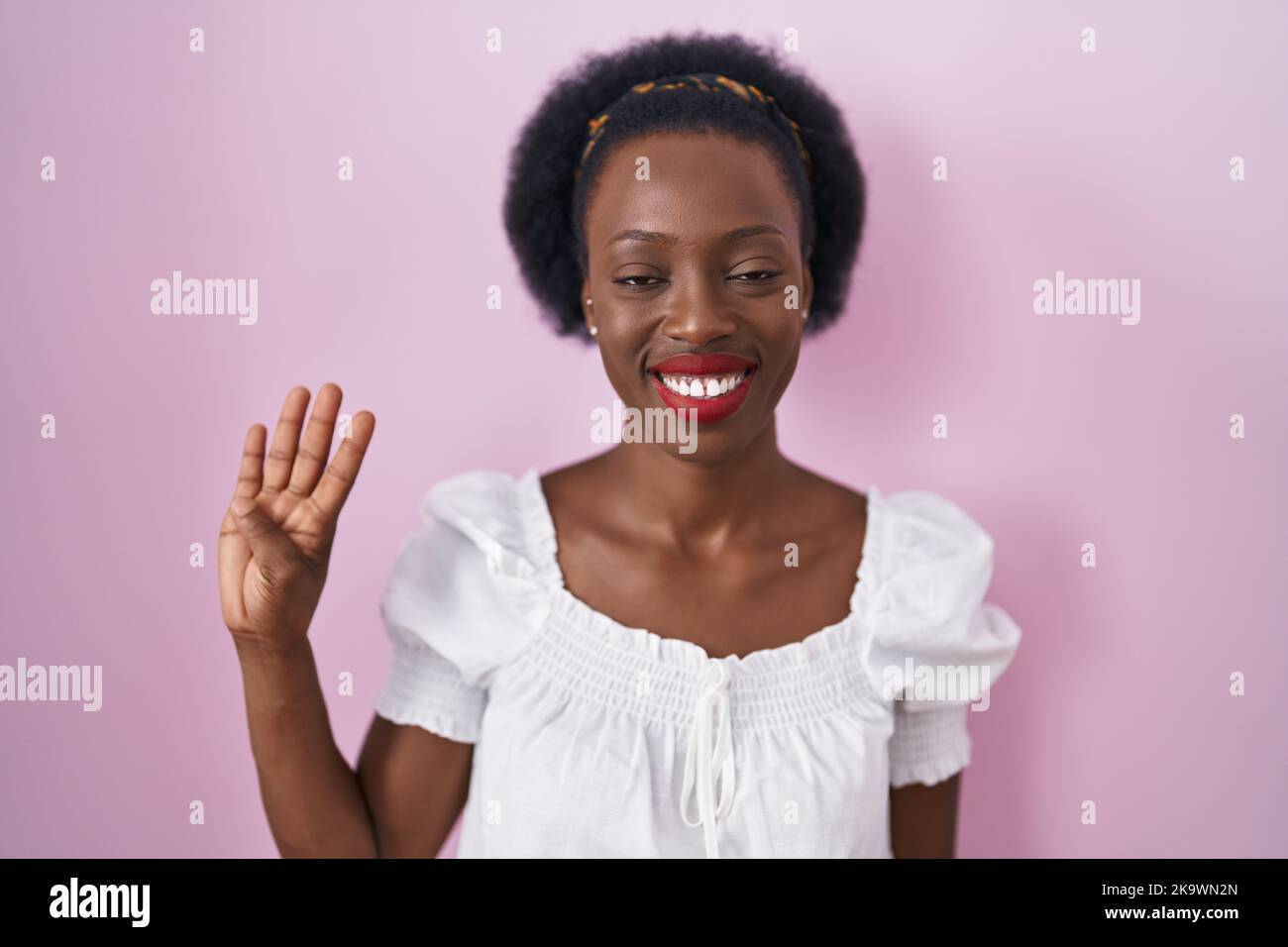 African woman with curly hair standing over pink background showing and ...