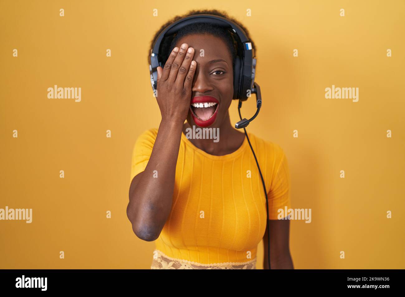 African woman with curly hair standing over yellow background wearing ...