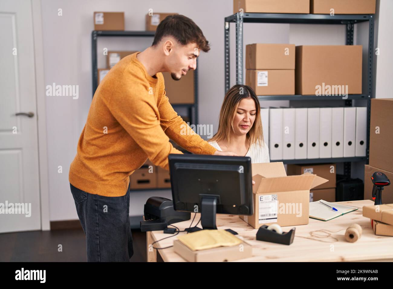 Young man and woman ecommerce business workers packing order at office ...
