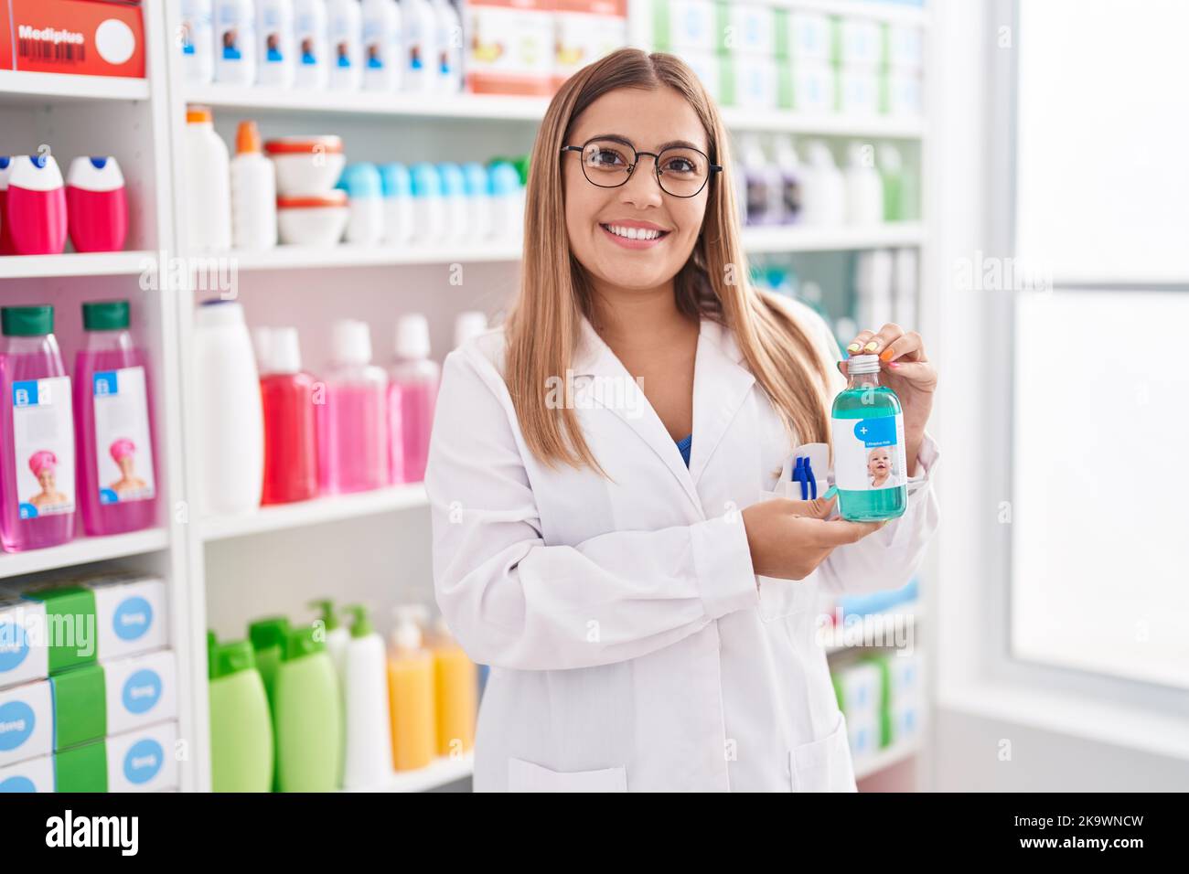 Young blonde woman working at pharmacy drugstore holding syrup smiling ...