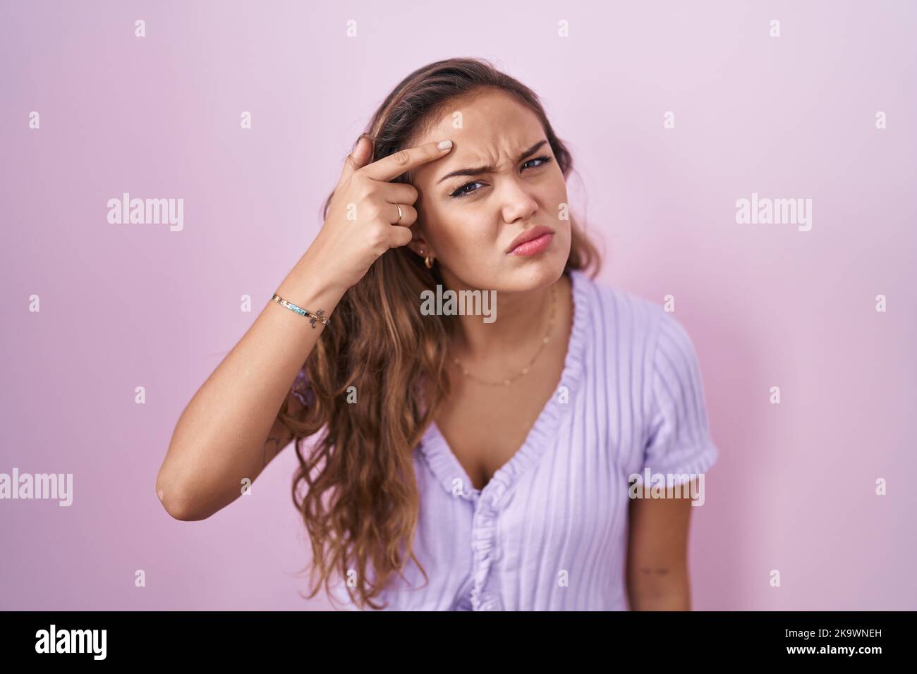 Young hispanic woman standing over pink background pointing unhappy to ...