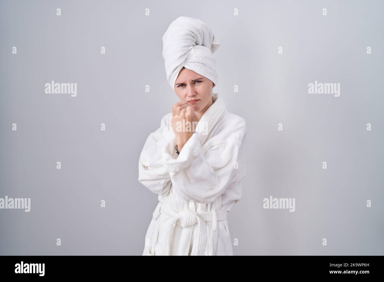 Blonde caucasian woman wearing bathrobe ready to fight with fist ...