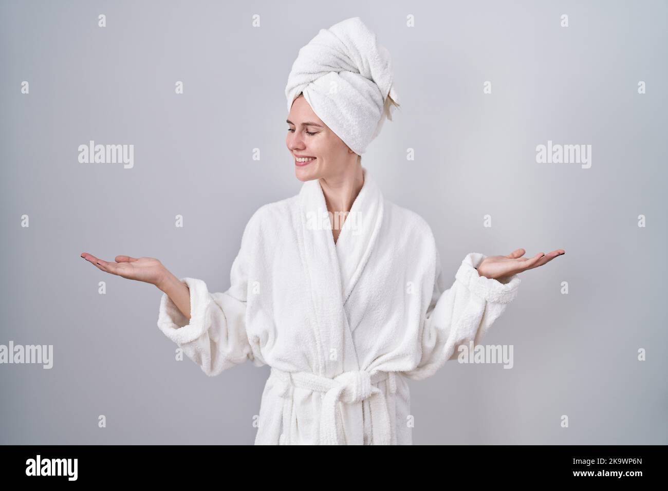 Blonde caucasian woman wearing bathrobe smiling showing both hands open ...