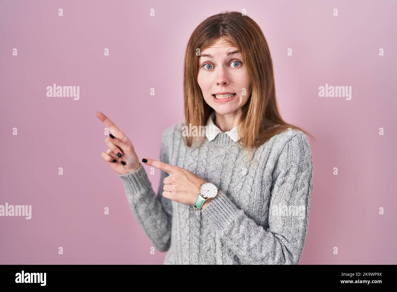 Beautiful woman standing over pink background pointing aside worried ...