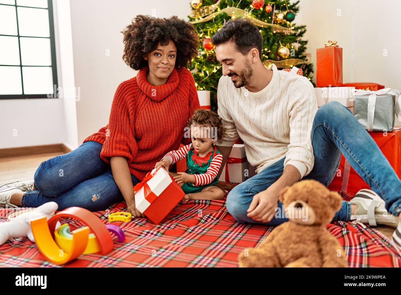 Couple and daughter playing with toys sitting by christmas tree at home ...