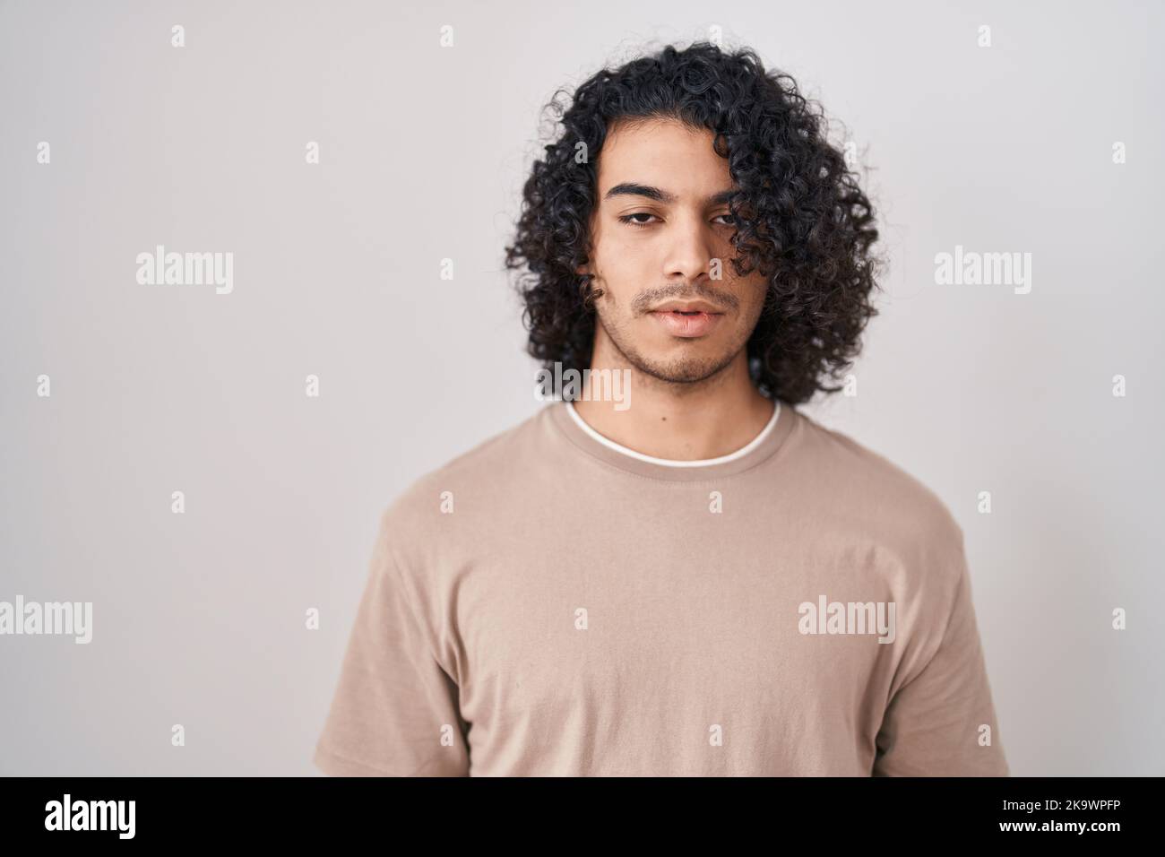 Hispanic man with curly hair standing over white background looking ...