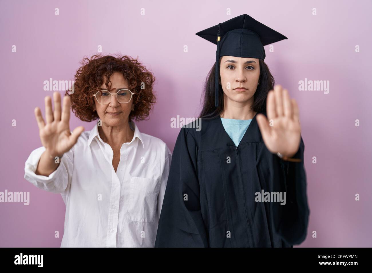 Hispanic mother and daughter wearing graduation cap and ceremony robe ...