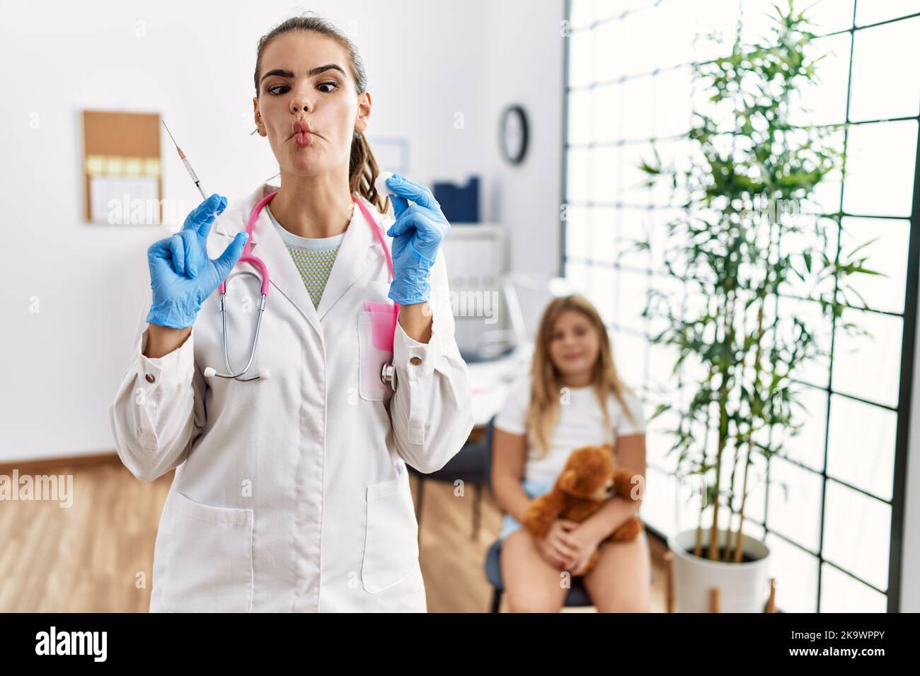 Young doctor woman putting vaccine to little girl making fish face with ...