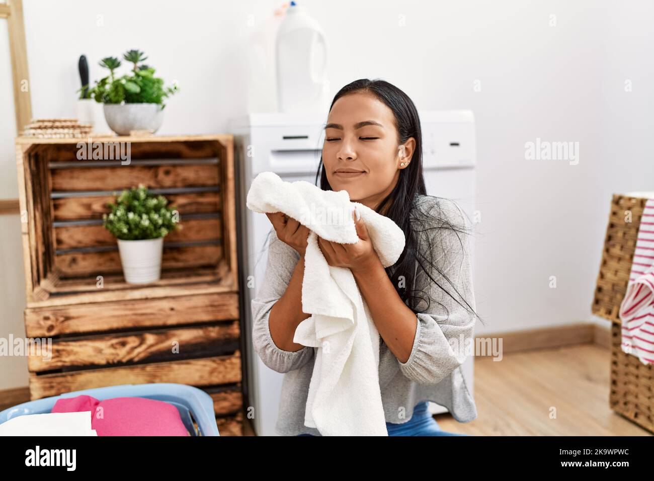 Young latin woman smiling confident smelling clothes at laundry room ...