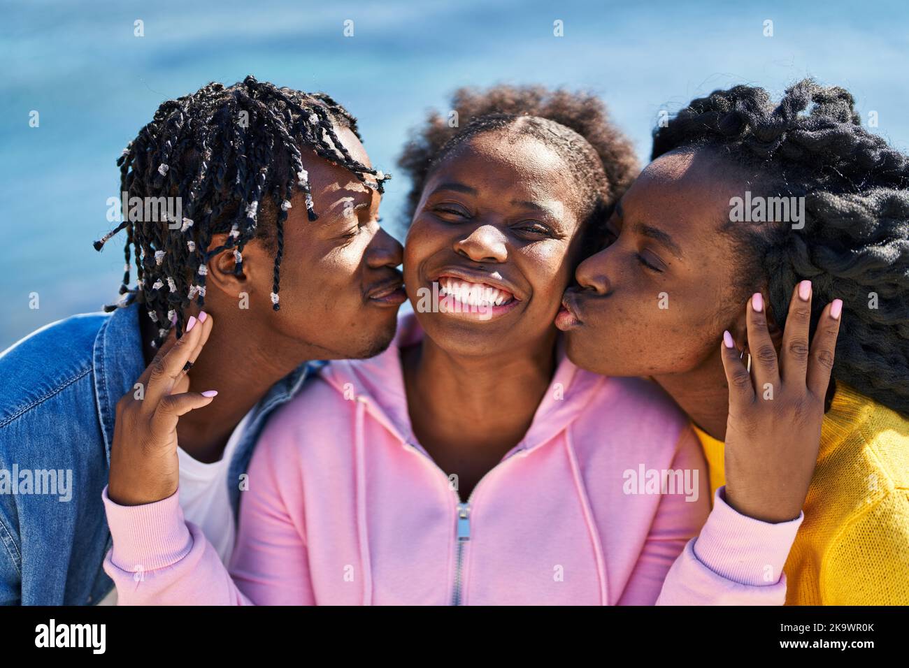 African american friends sitting on bench together kissing at seaside ...