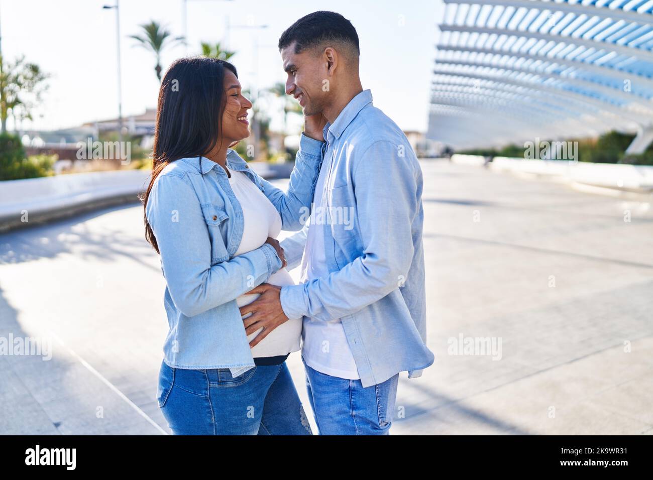 Young latin couple expecting baby standing together touching belly at ...