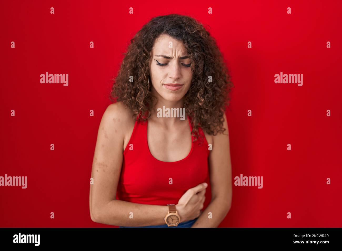 Hispanic woman with curly hair standing over red background with hand ...