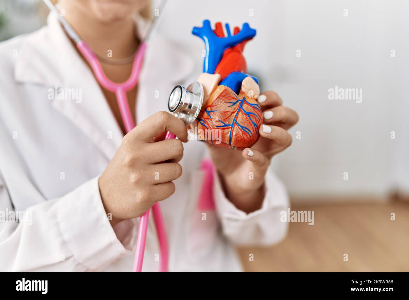 Young blonde girl wearing doctor uniform auscultate heart at clinic ...