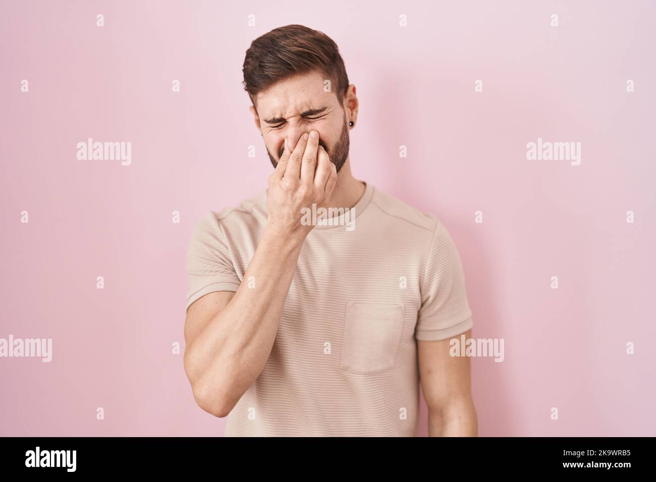 Hispanic man with beard standing over pink background smelling ...
