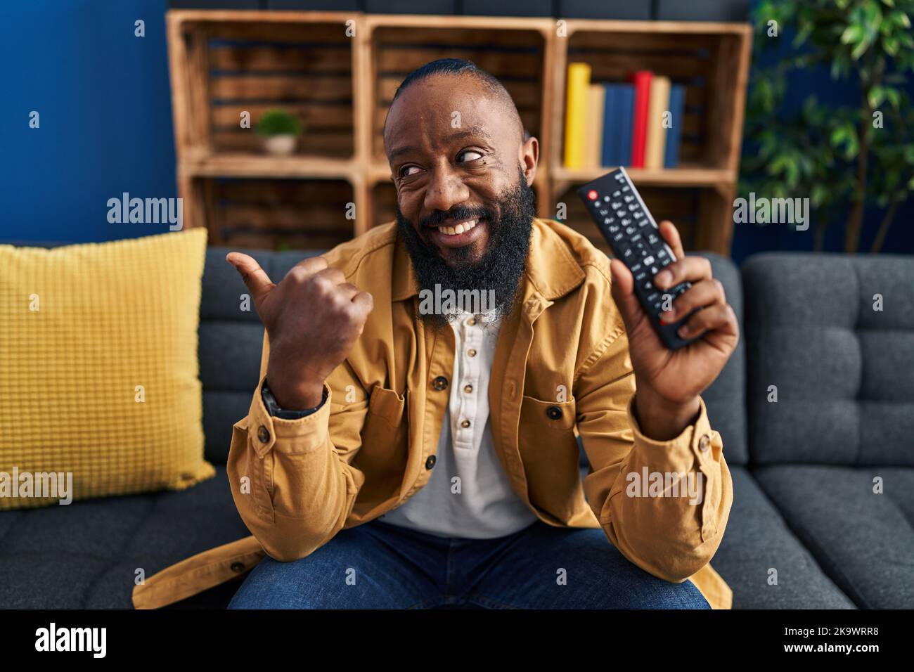 African american man holding television remote control pointing thumb ...