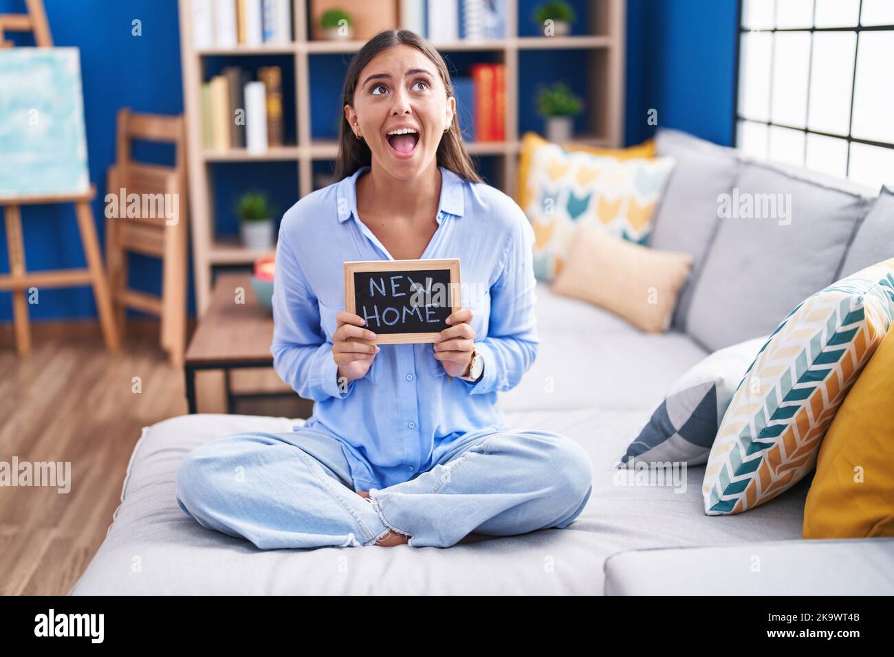 Young hispanic woman holding blackboard with new home text sitting on ...
