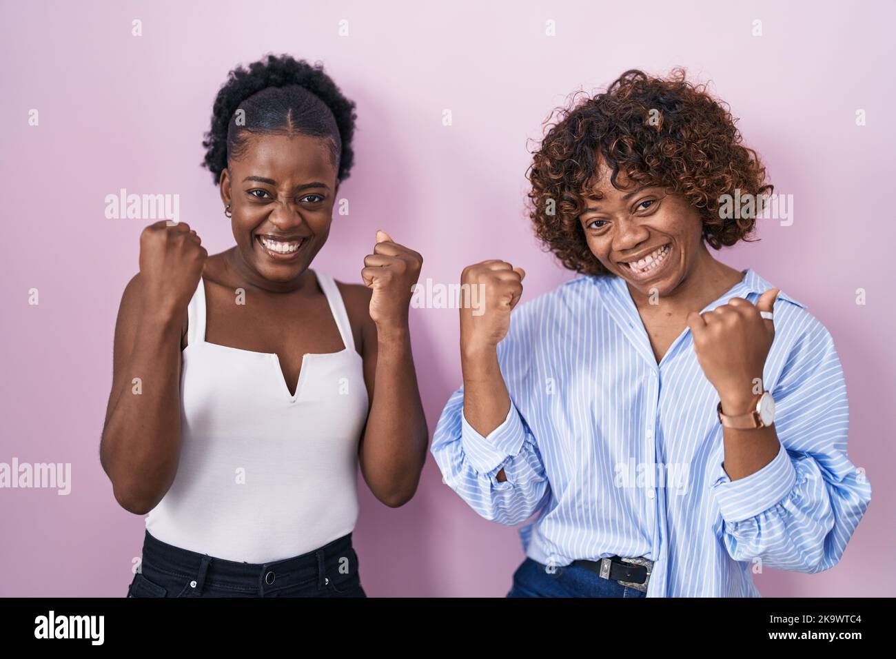 Two african women standing over pink background very happy and excited ...