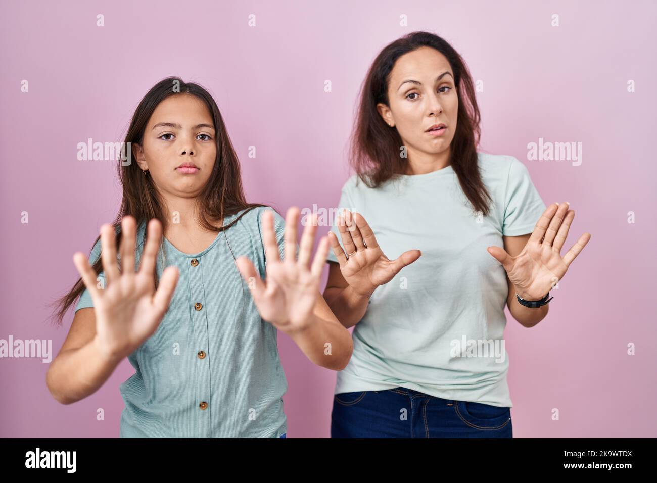 Young mother and daughter standing over pink background moving away ...