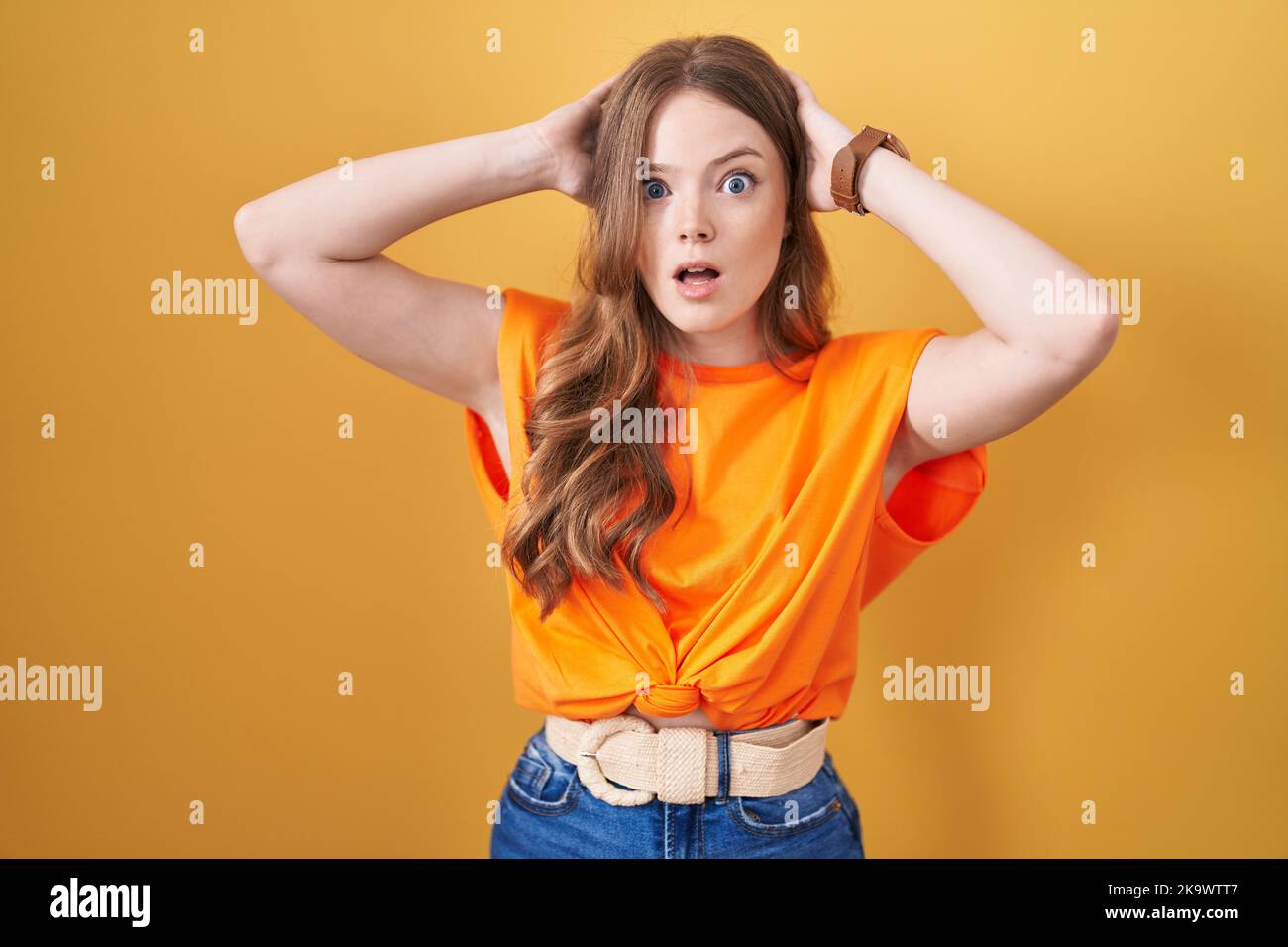 Caucasian woman standing over yellow background crazy and scared with ...