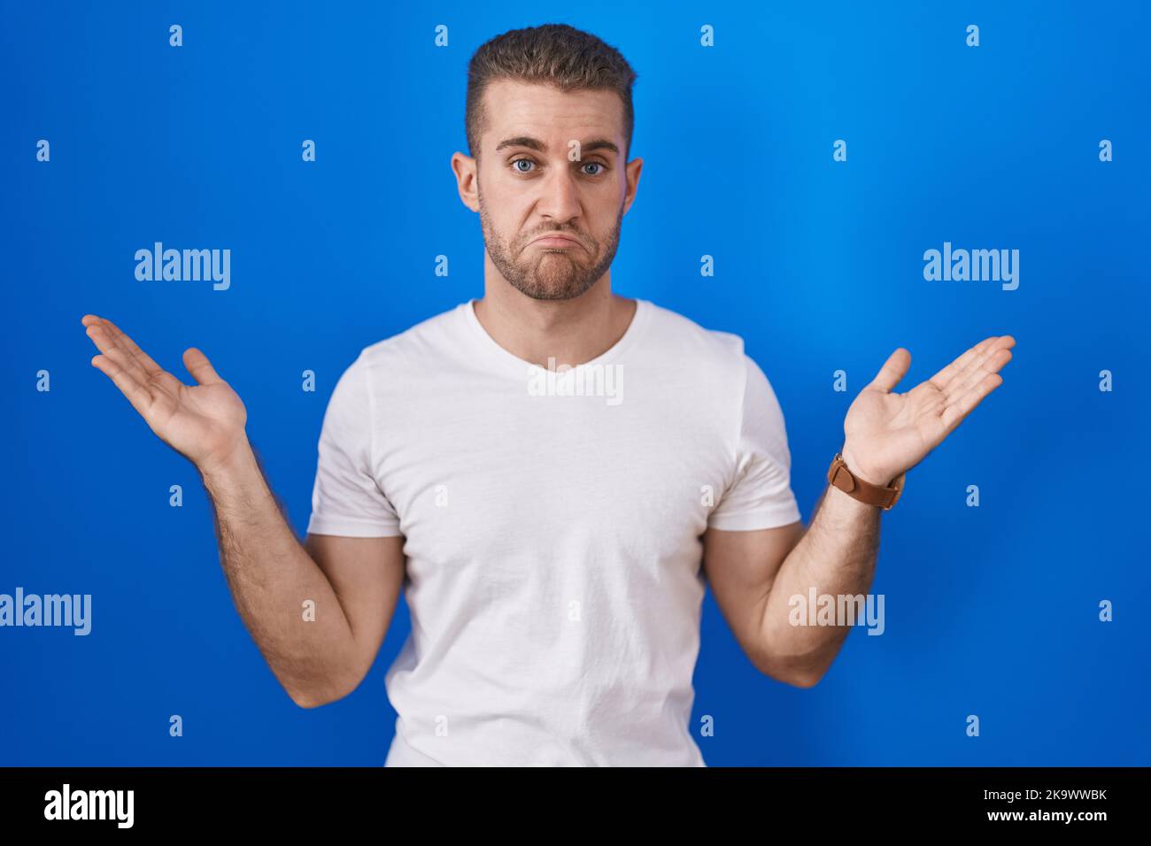 Young caucasian man standing over blue background clueless and confused ...