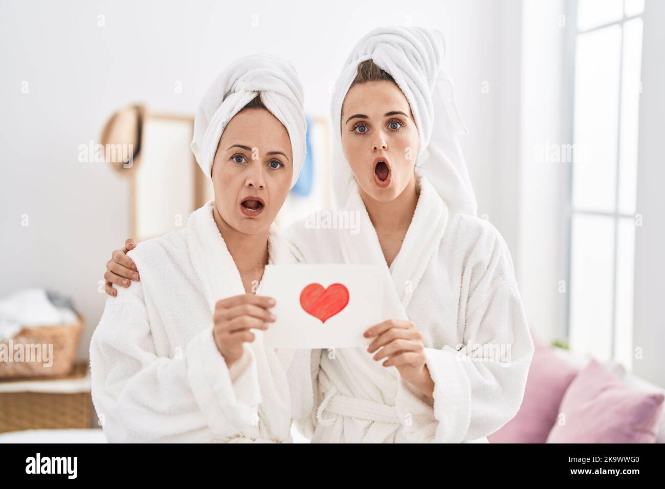 Middle age woman and daughter wearing bath robe holding heart card ...