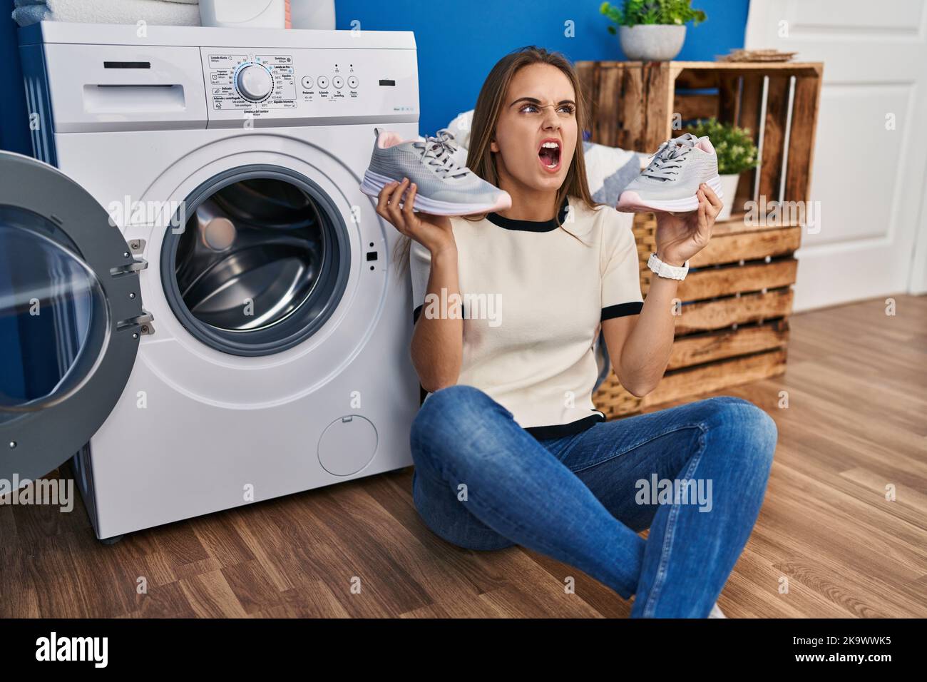 Young woman putting sneakers in washing machine angry and mad screaming ...