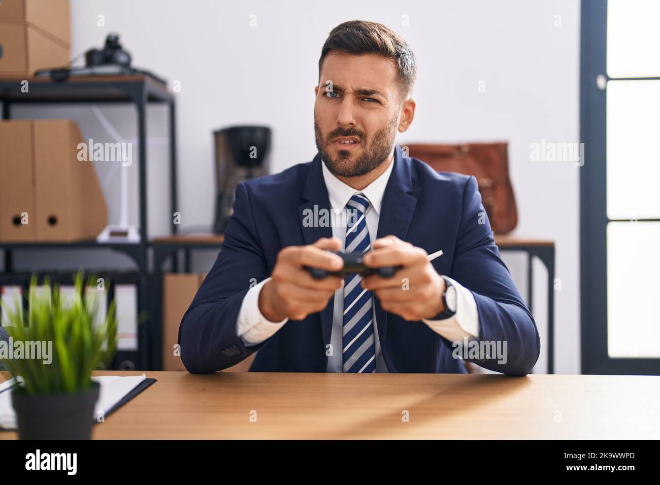 Handsome hispanic man playing video games at the office clueless and ...