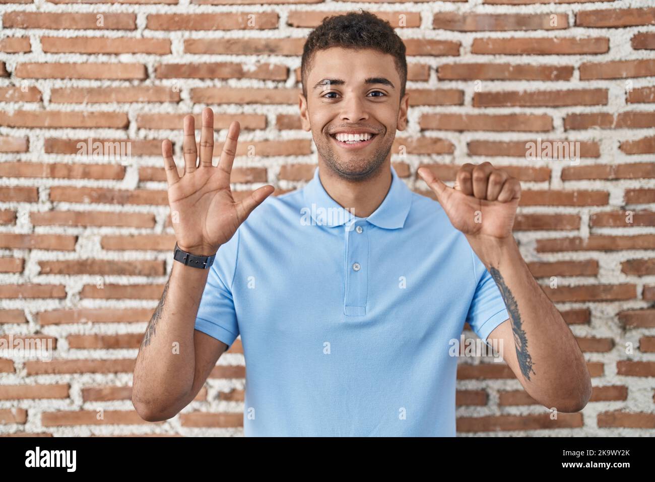 Brazilian young man standing over brick wall showing and pointing up ...