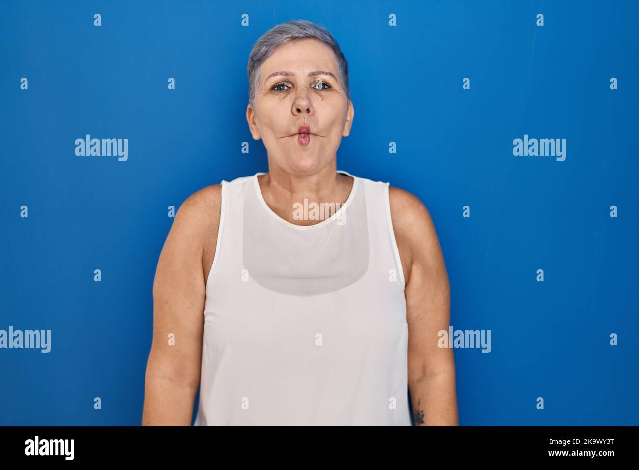Middle age caucasian woman standing over blue background making fish ...