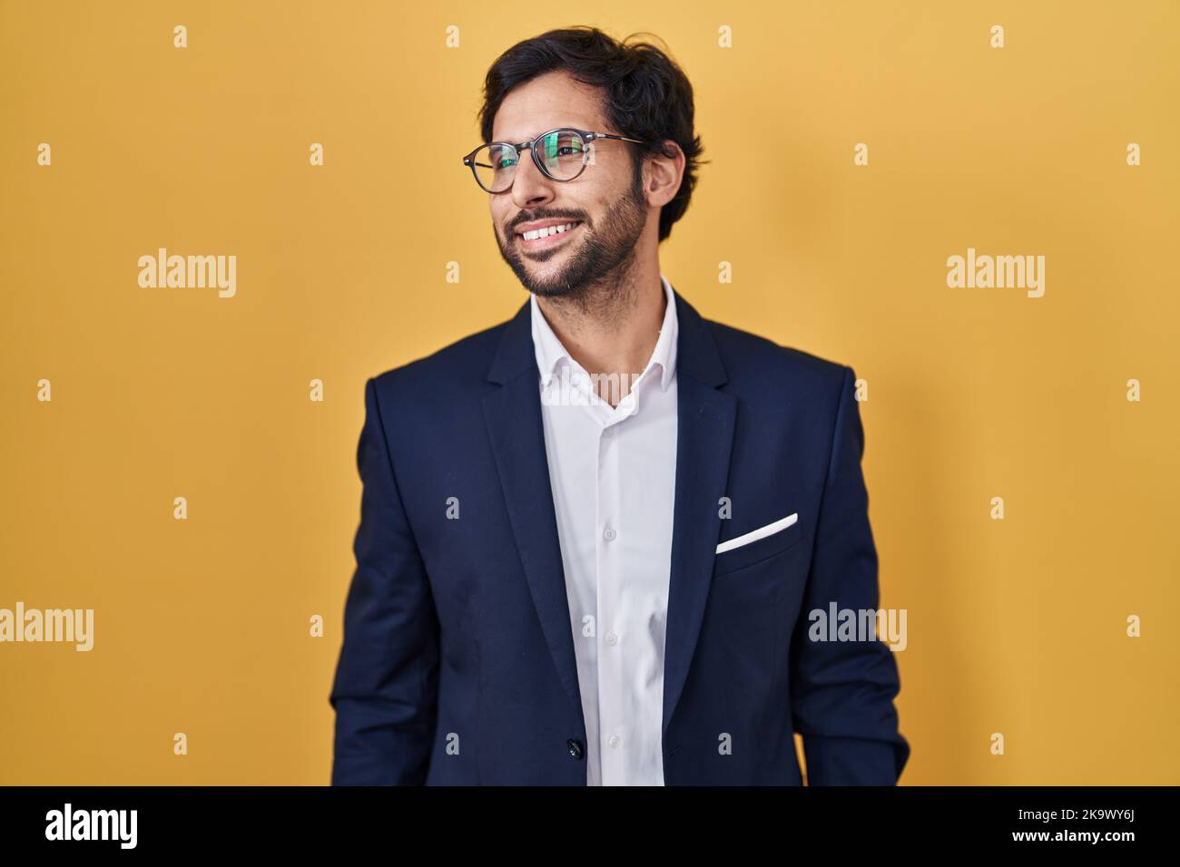 Handsome latin man standing over yellow background looking away to side ...