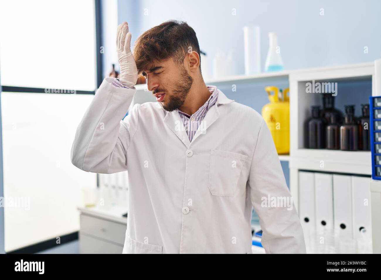 Arab man with beard working at scientist laboratory surprised with hand on head for mistake ...