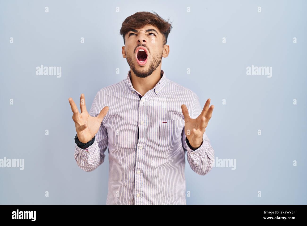 Arab man with beard standing over blue background crazy and mad ...