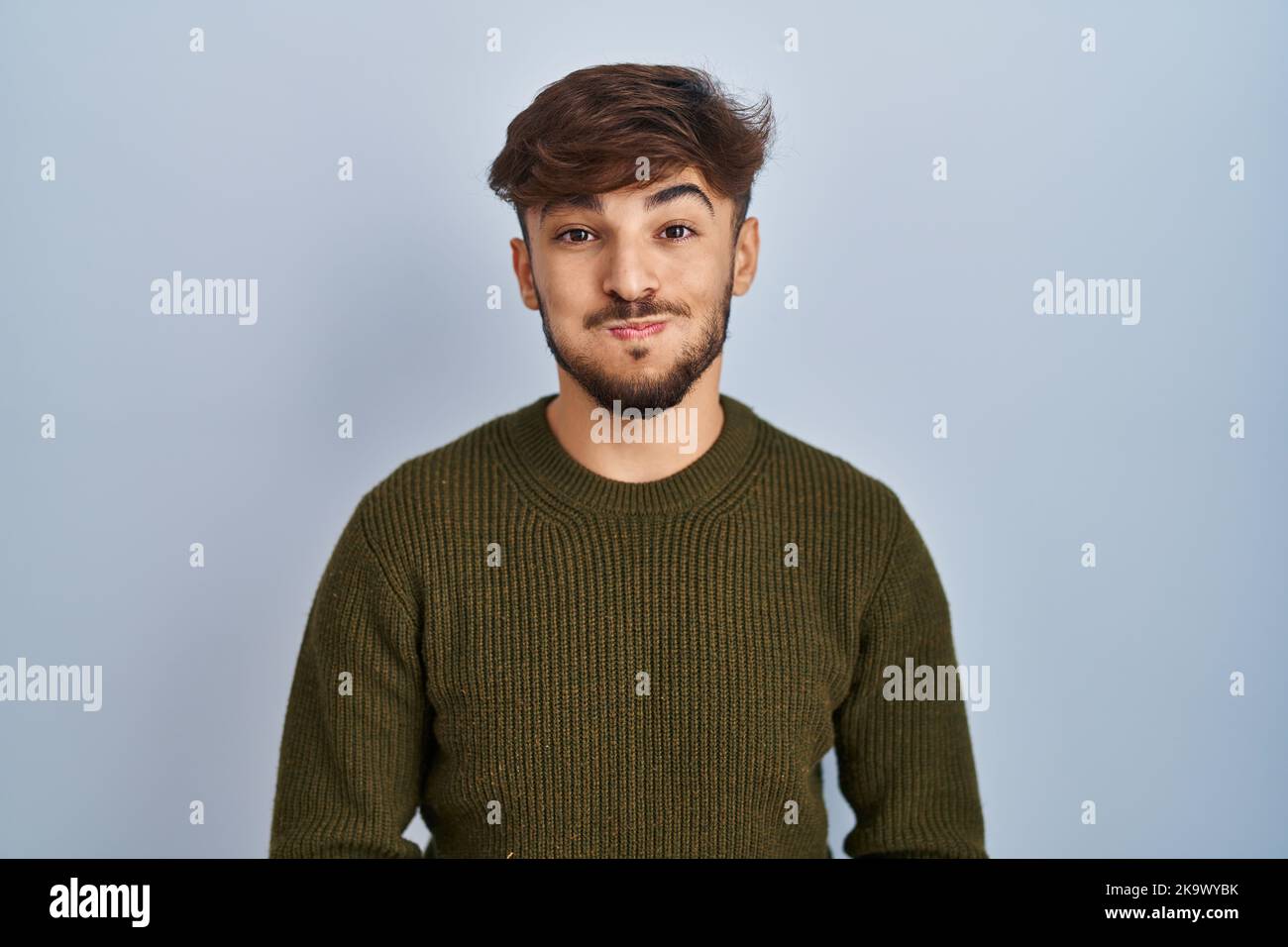 Arab man with beard standing over blue background puffing cheeks with ...