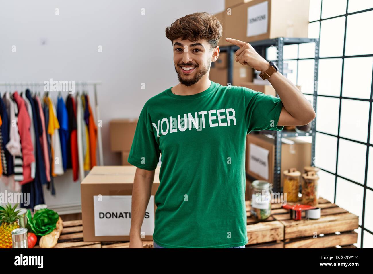Young arab man wearing volunteer t shirt at donations stand smiling ...