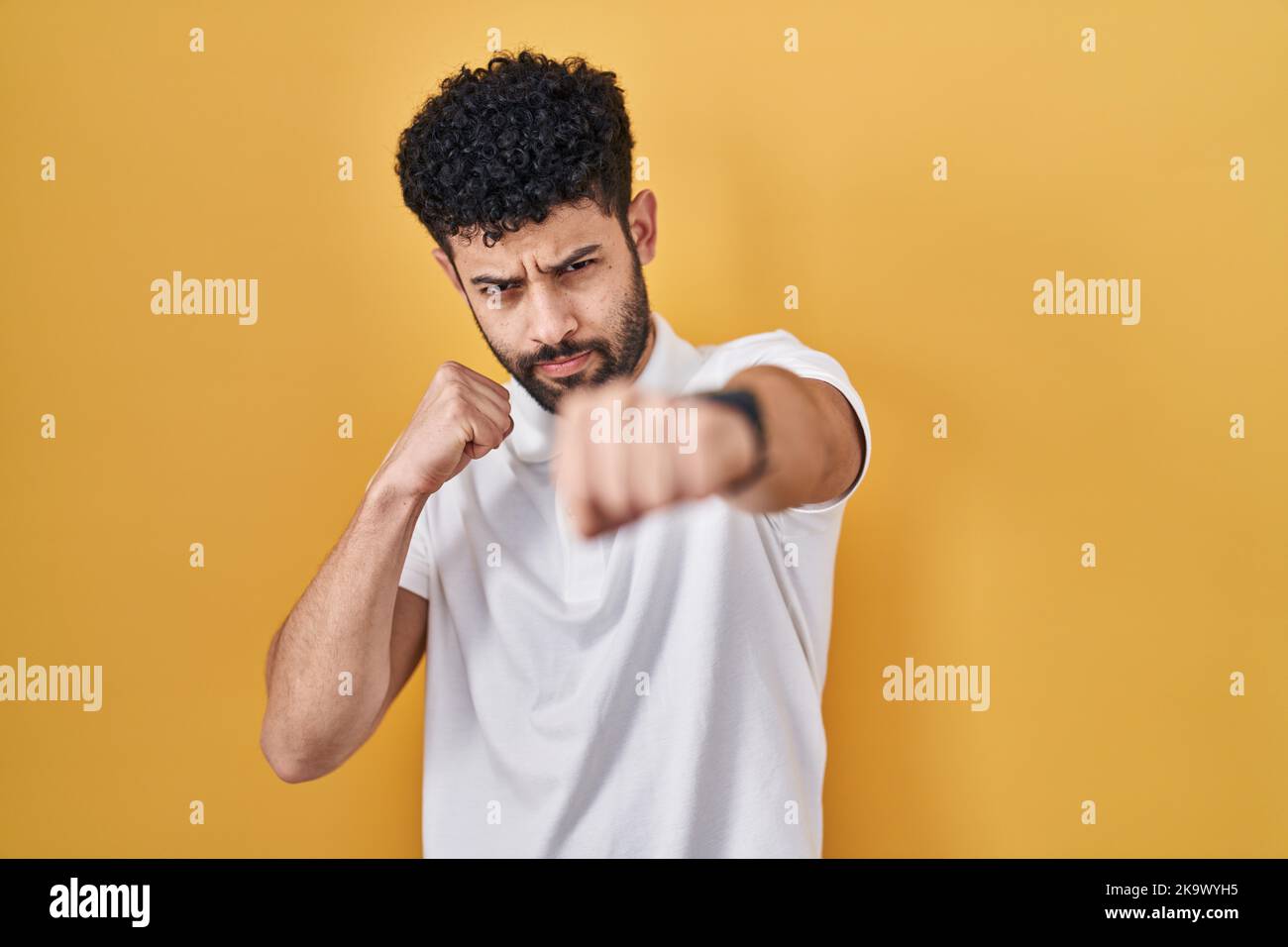 Arab man standing over yellow background punching fist to fight ...