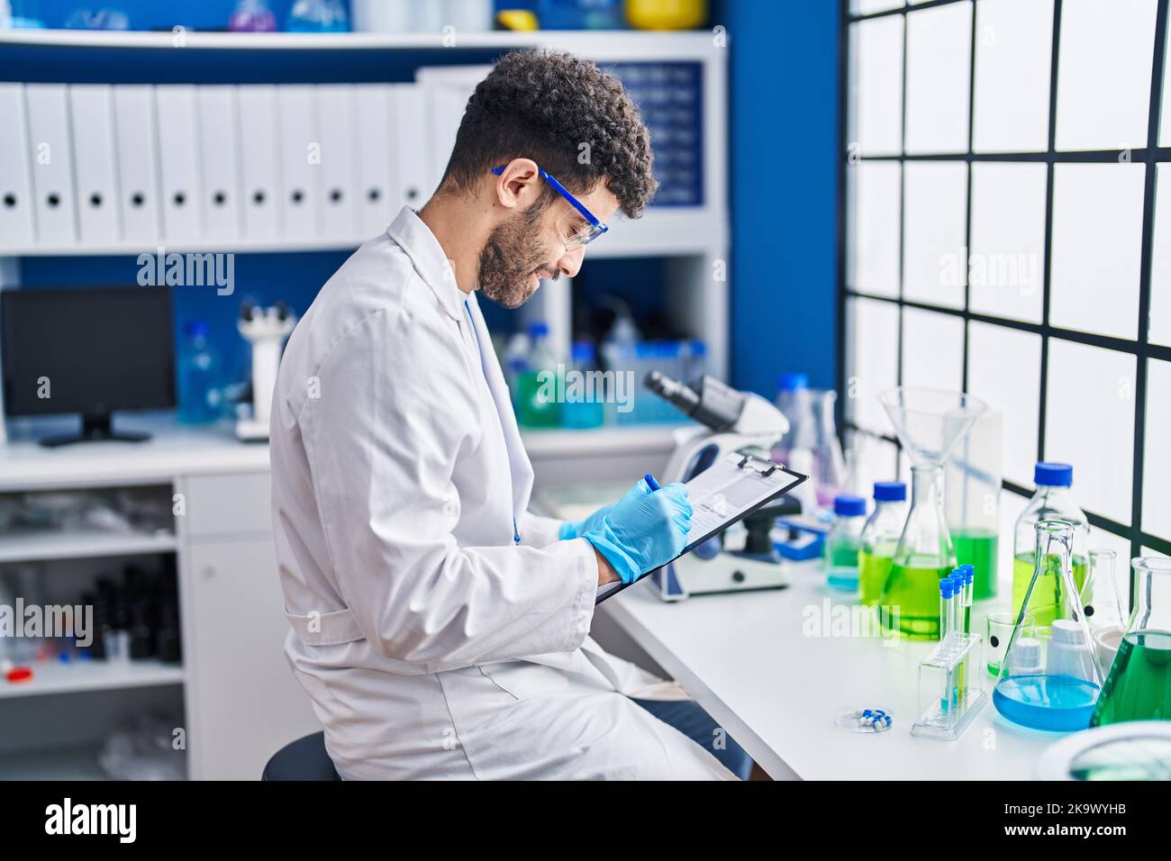 Young arab man wearing scientist uniform writing on clipboard at ...