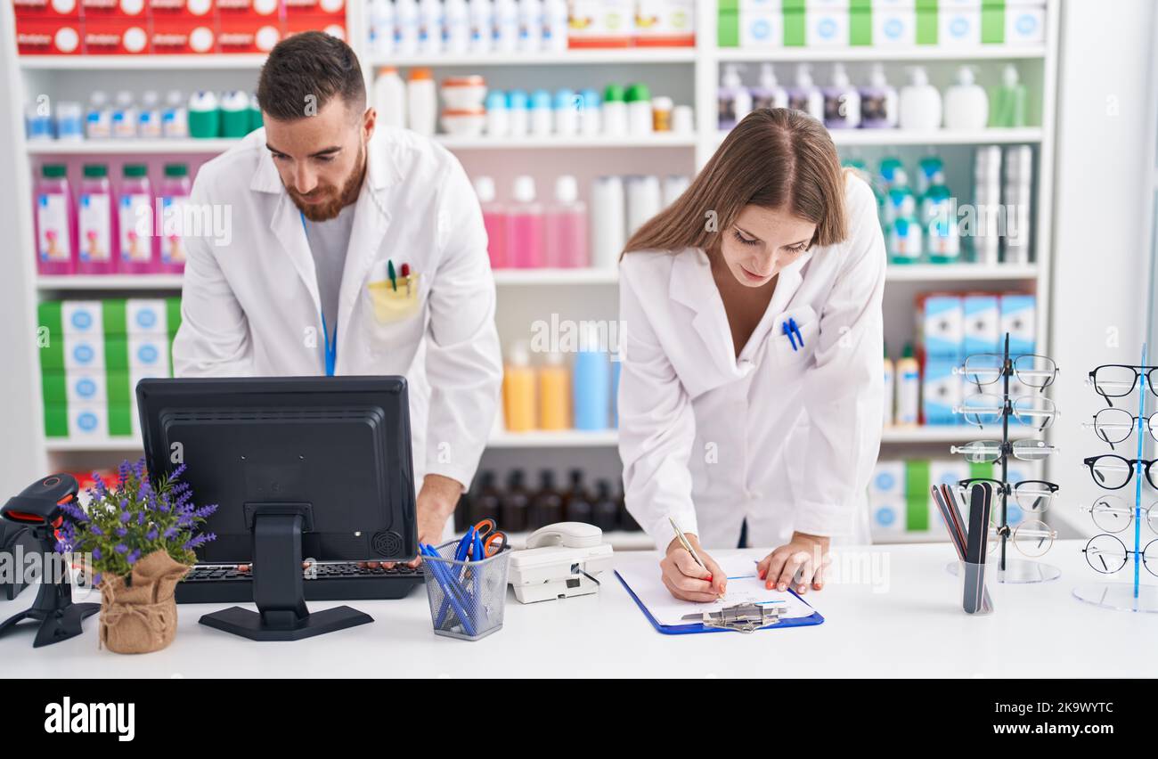 Man and woman pharmacists using computer writing on document at ...
