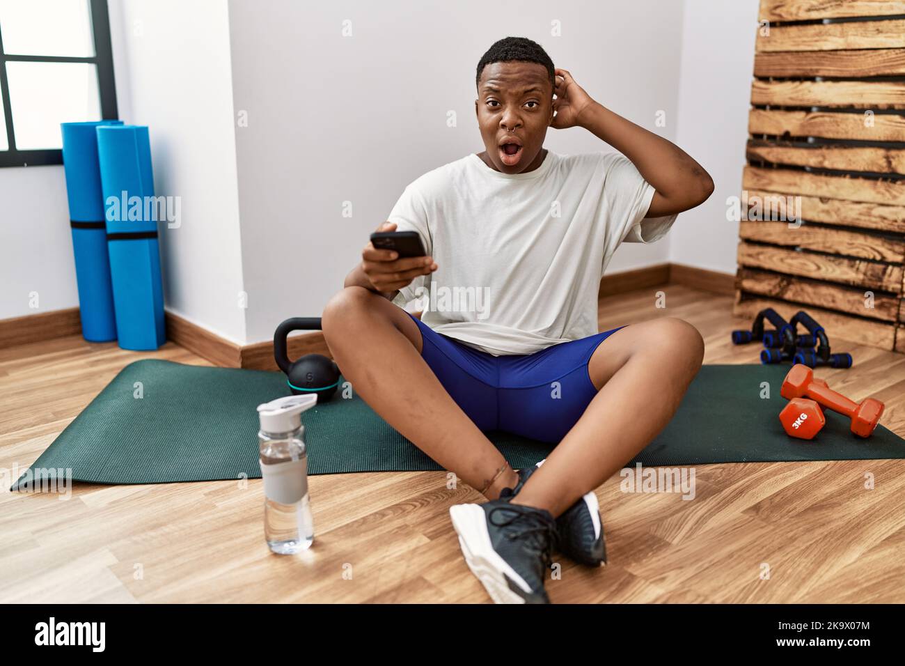 Young african man sitting on training mat at the gym using smartphone ...