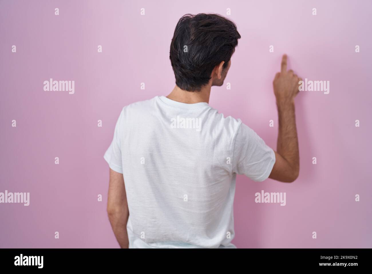 Young hispanic man standing over pink background posing backwards ...