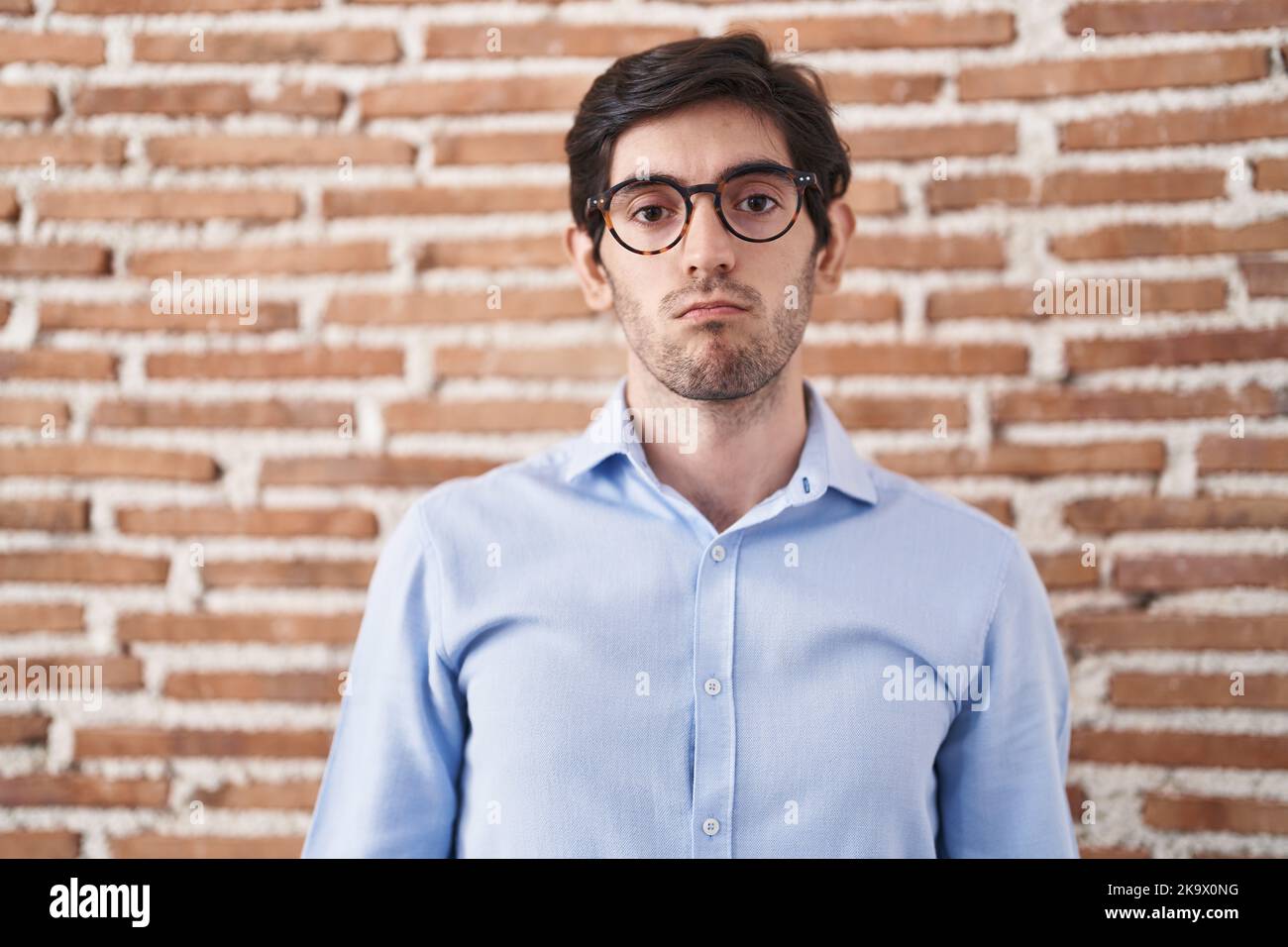 Young hispanic man standing over brick wall background depressed and ...