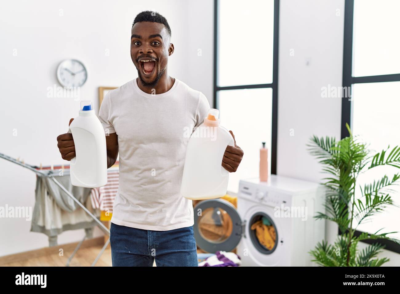 Young african man doing laundry holding detergent bottles celebrating ...