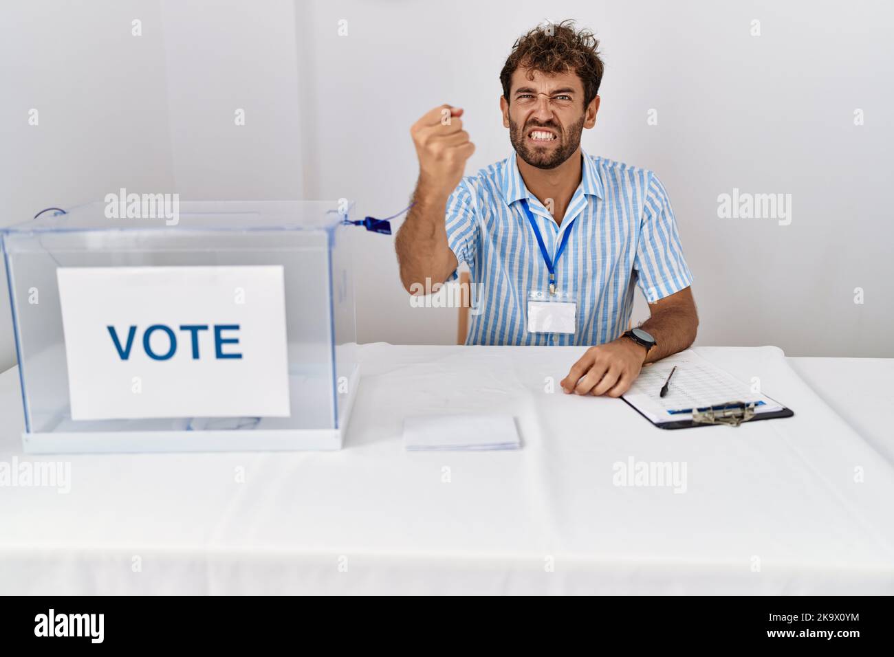 Young handsome man at political election sitting by ballot angry and ...