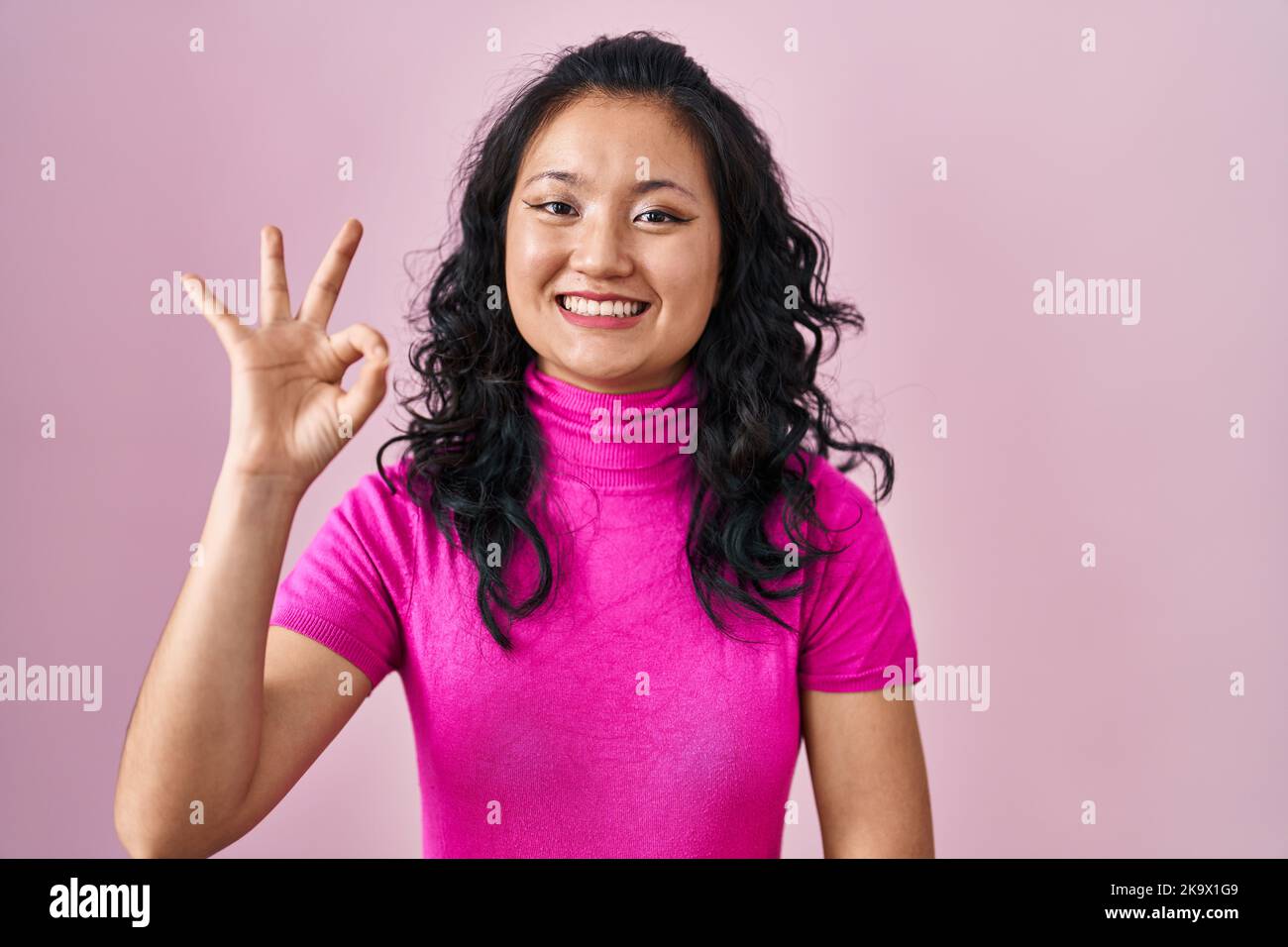 Young asian woman standing over pink background smiling positive doing ...